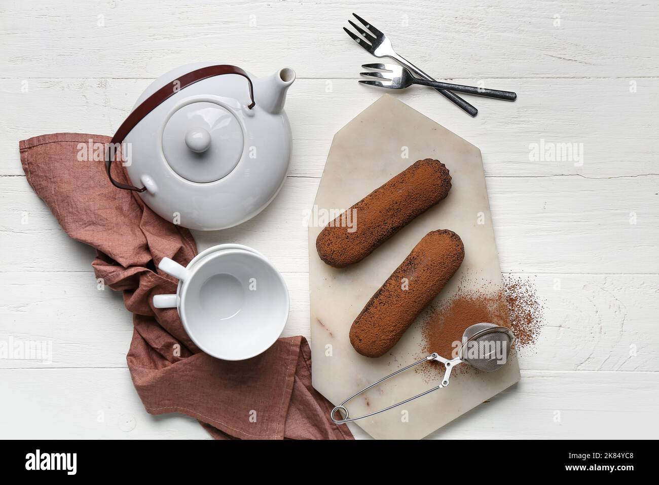 Board with tasty chocolate eclairs and tea set on white wooden ...