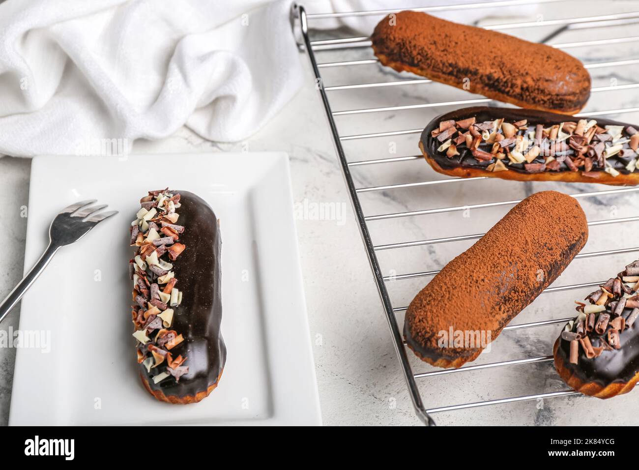 Plate and grid with tasty chocolate eclairs on light background ...