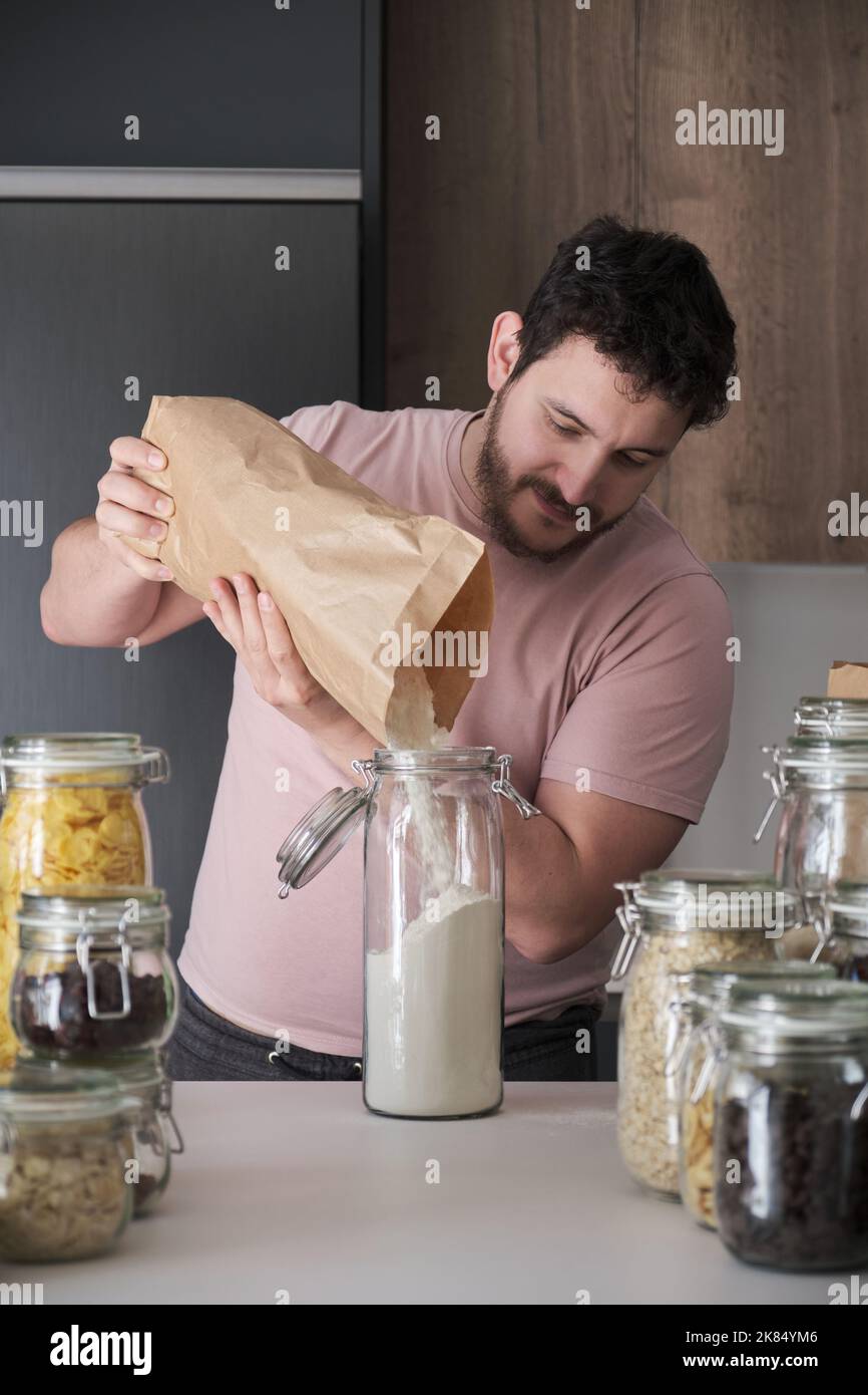 Young latin man filling up a jar with wheat flour from a paper bag ...