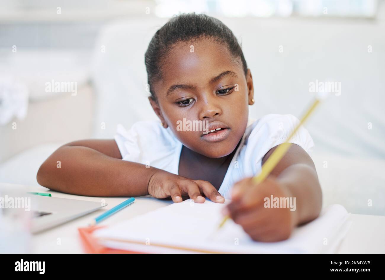 Focused on finishing homework. a little girl writing in a book at home ...