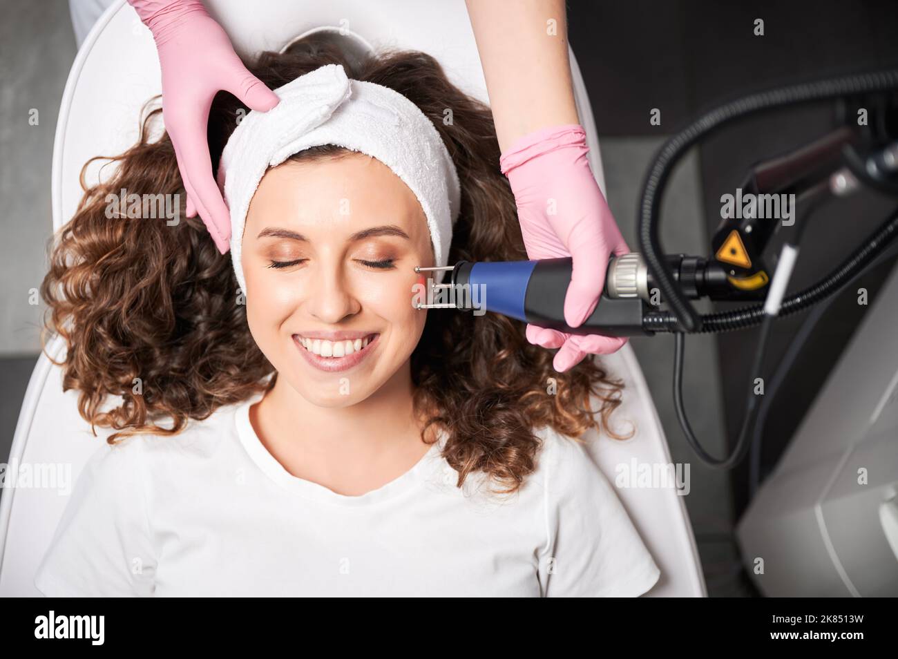 Top view of smiling woman with closed eyes receiving facial skincare ...