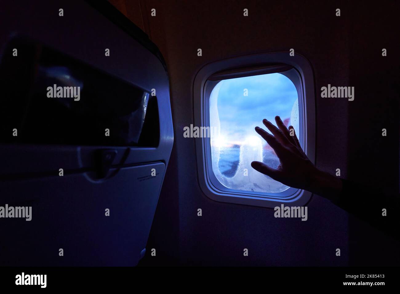 Female hand touches the warm sun rays from airplane window. Woman ...