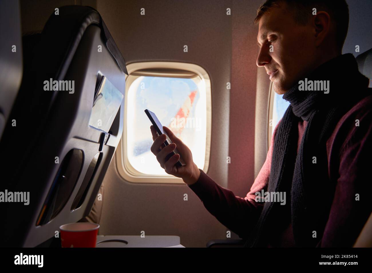 Businessman sitting next to airplane window and using smartphone. Man ...