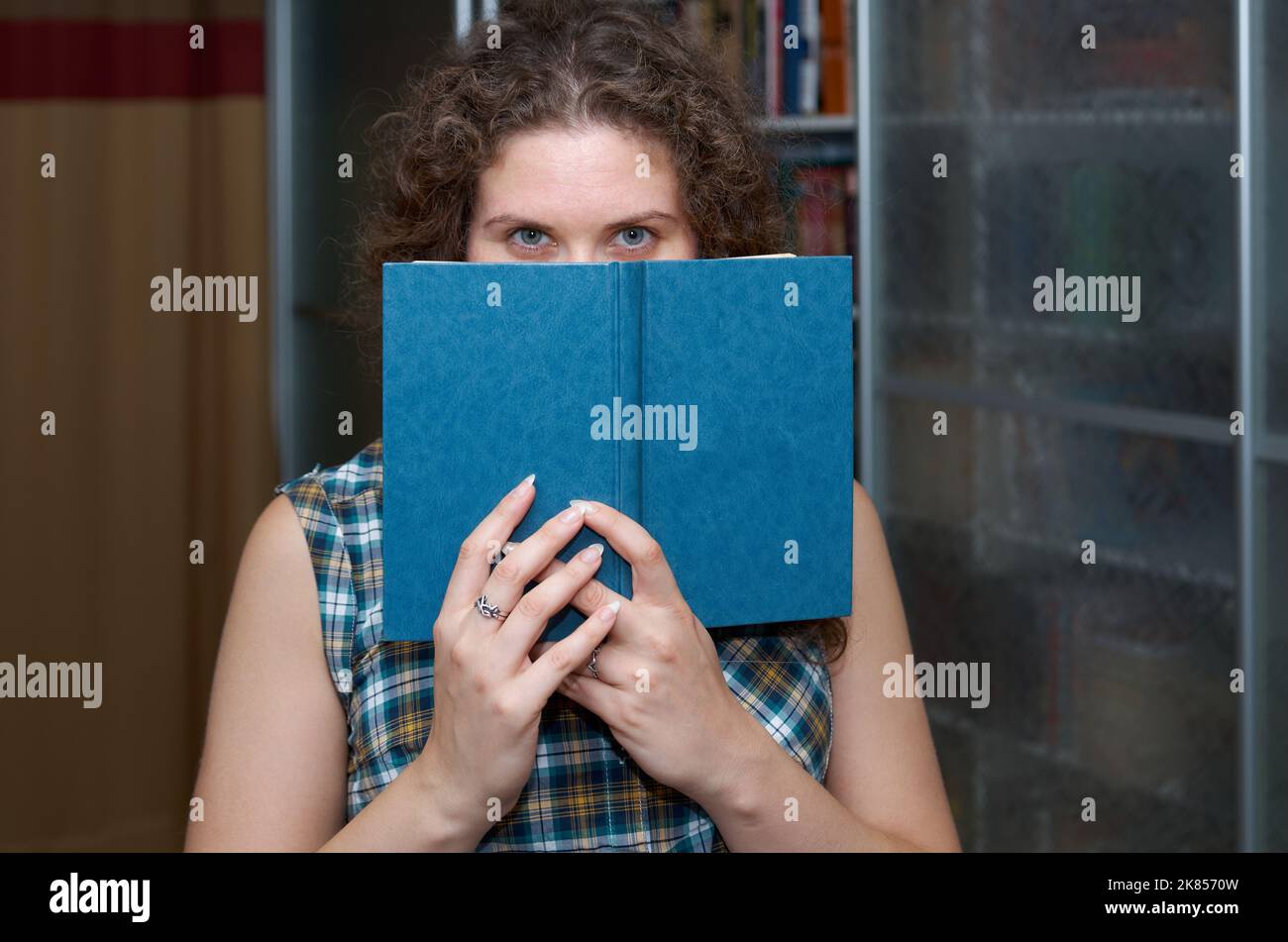 Woman reading a book standing by a bookcase Stock Photo - Alamy