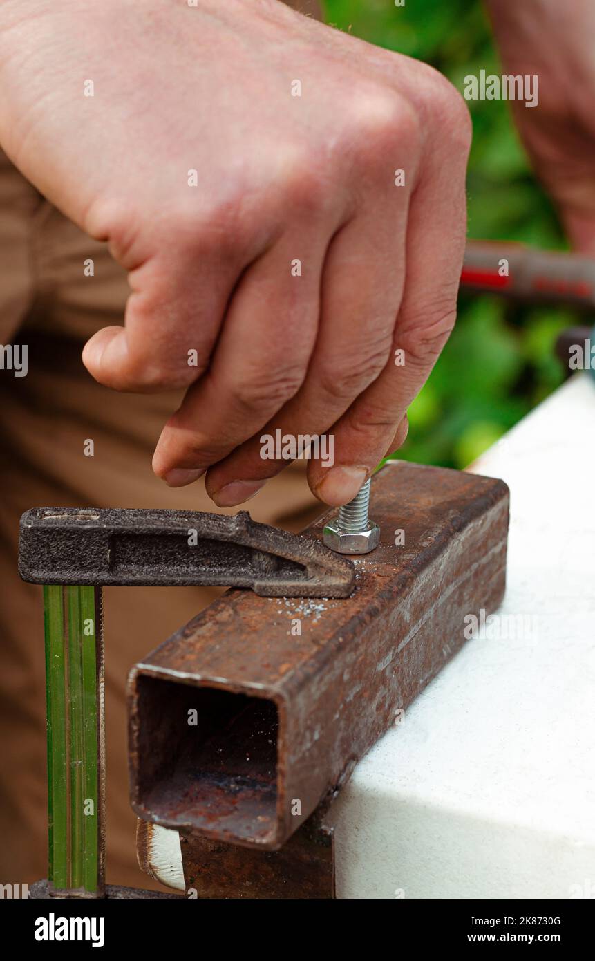 A man's hand screws a bolt into a metal nut. Working with metal Stock ...