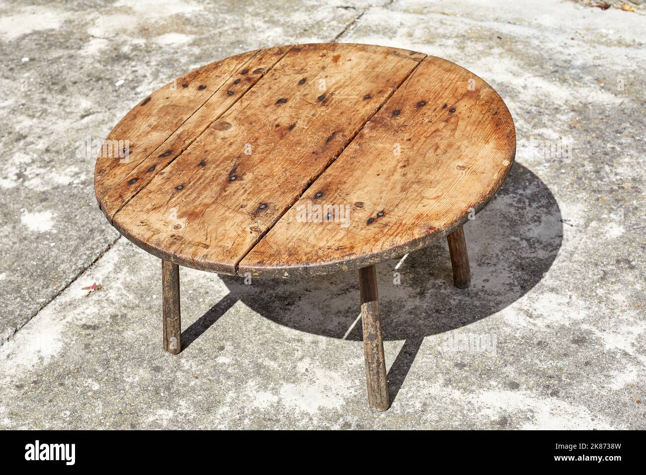 Handmade wooden table with three legs, in a concrete paved courtyard ...