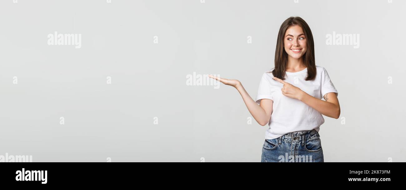 Attractive young woman pointing finger at something she holding on hand ...