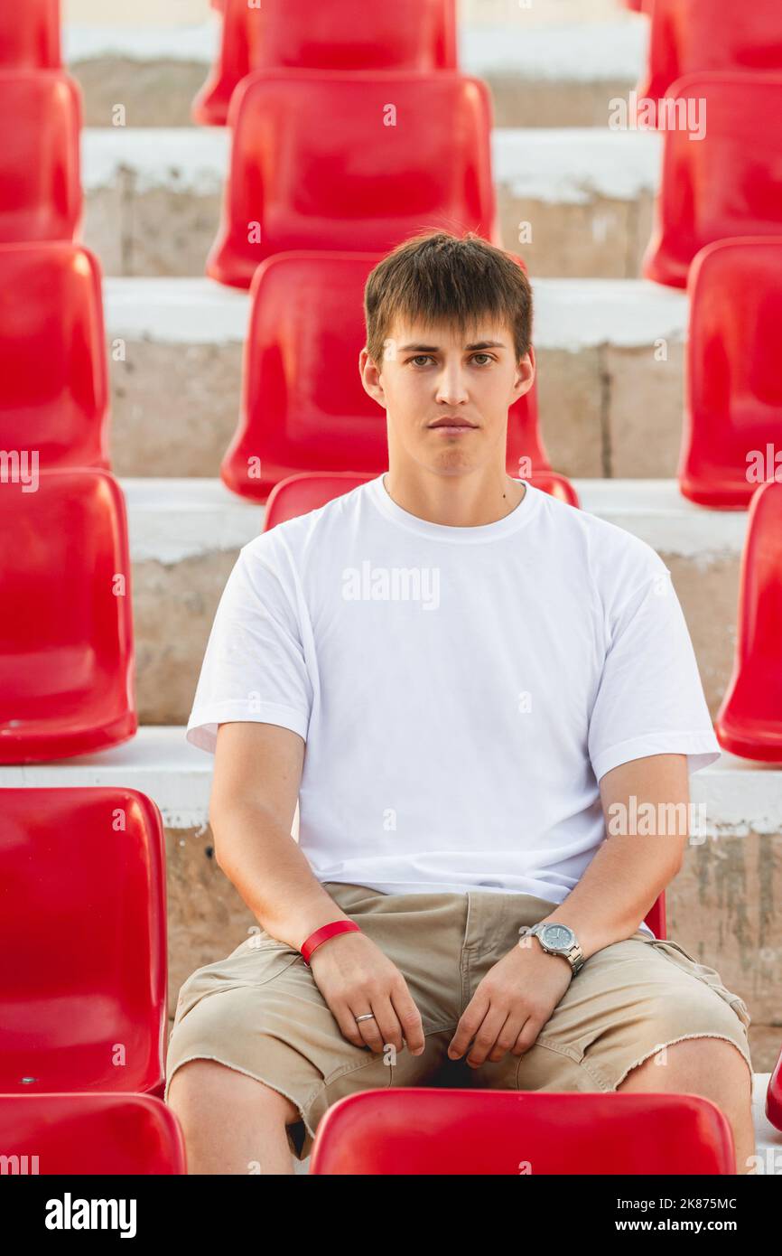 Bored young man sitting in deserted audience with bright red seats ...