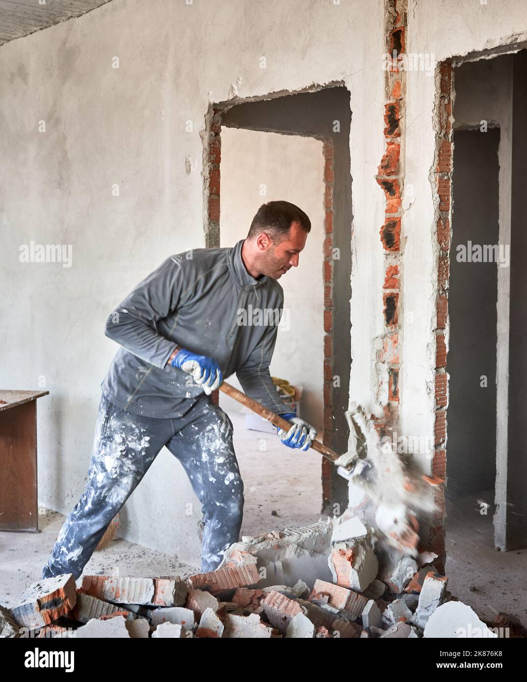 Man builder using sledgehammer while breaking the wall between two ...