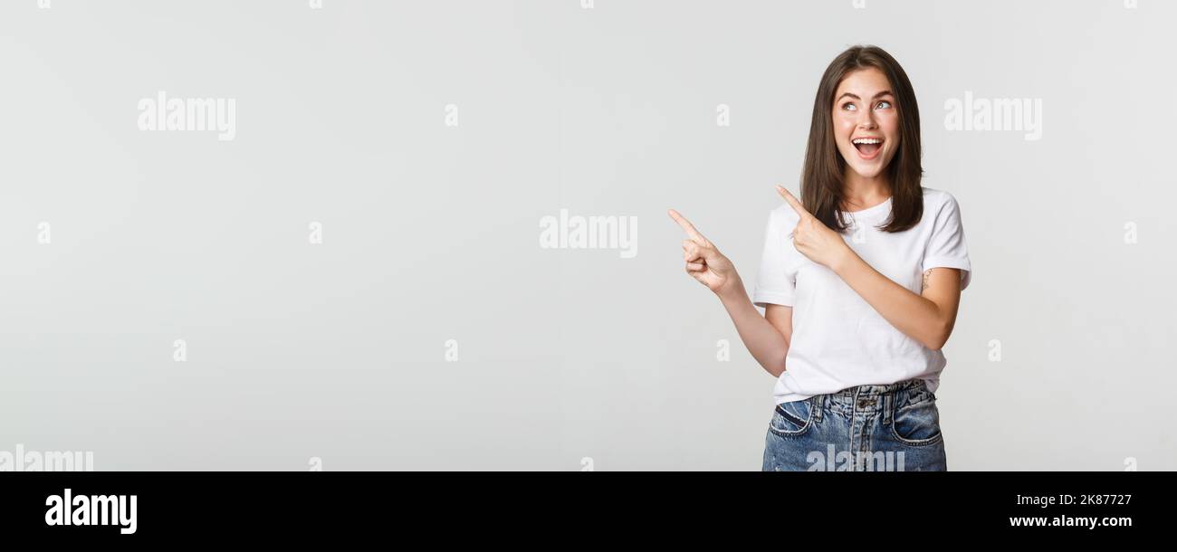 Attractive smiling brunette girl pointing fingers upper left corner ...