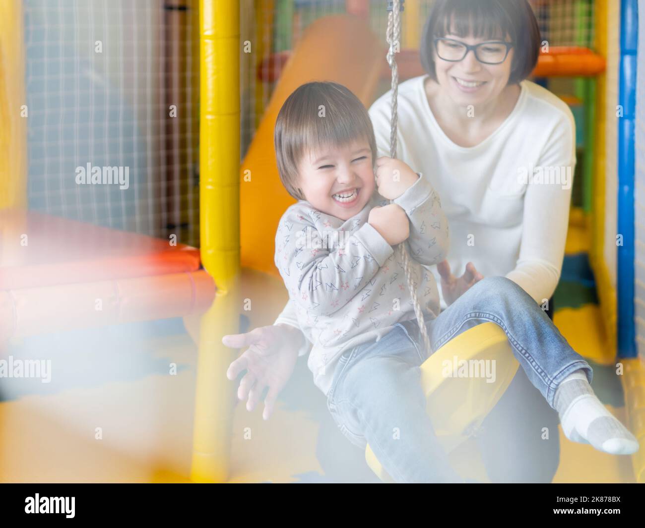Toddler plays on rope swing with his mother or babysitter. Physical ...