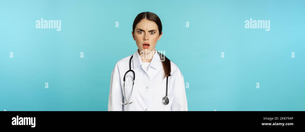 Portrait of shocked woman doctor, female hospital intern in white coat ...