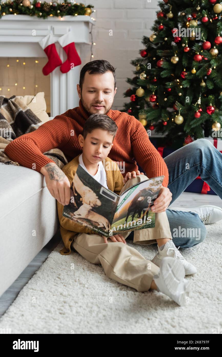 father and son sitting on floor in living room and reading magazine ...