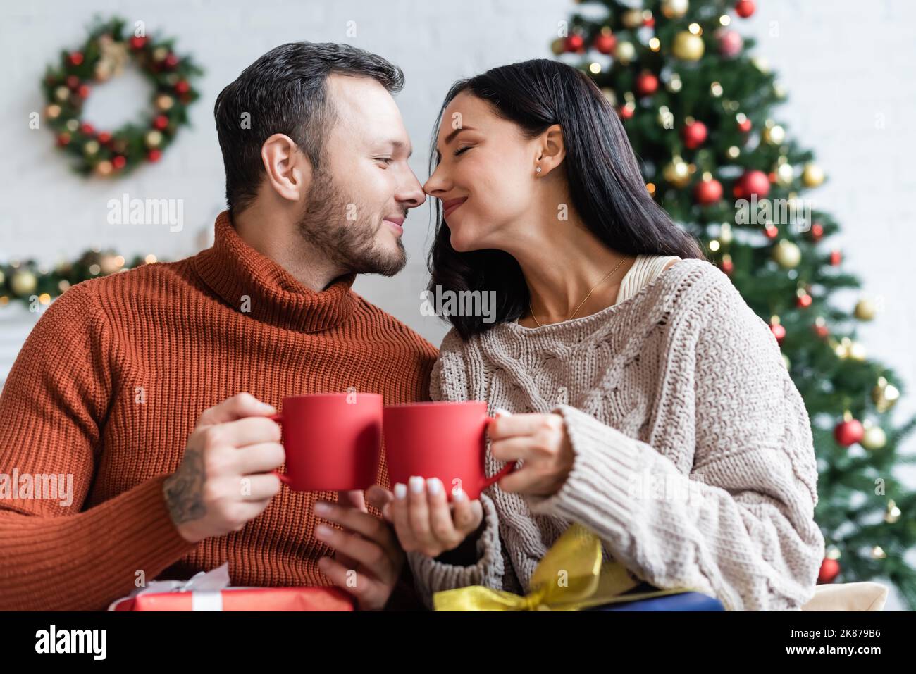 joyful couple with cups of warm cocoa sitting face to face near ...