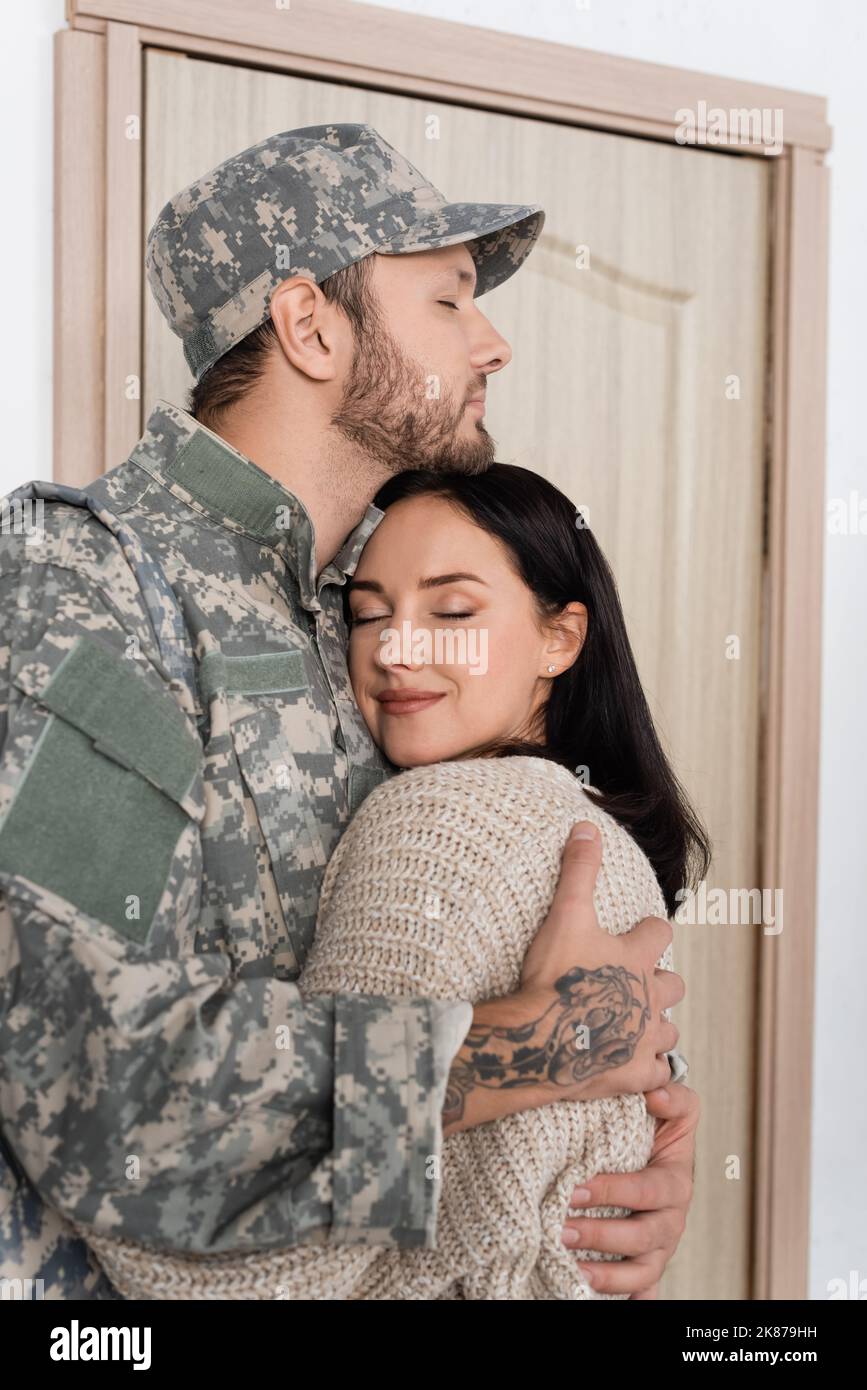 bearded man in military uniform hugging happy wife while coming back ...