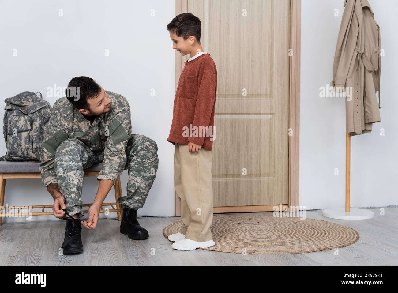 smiling boy looking at dad in military uniform unlacing boot while ...