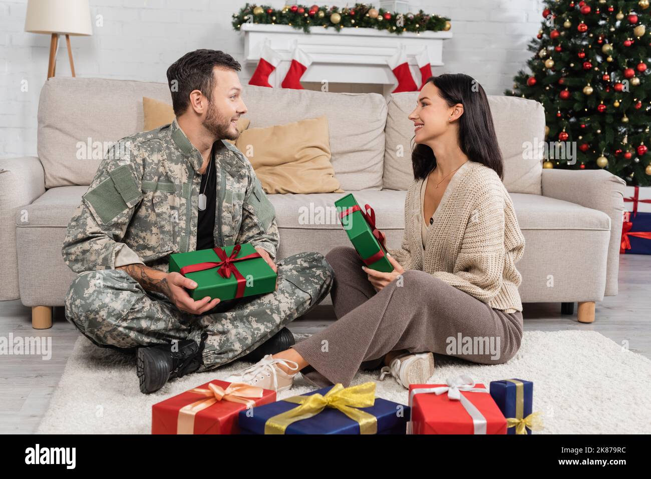 military man with happy wife sitting on floor near gift boxes and ...
