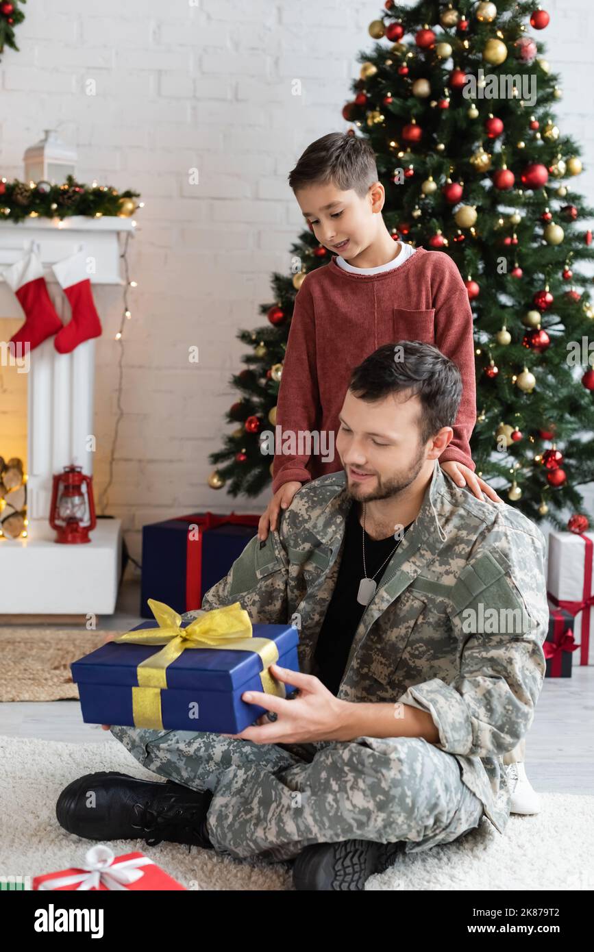 happy military man holding new year present near son and blurred ...