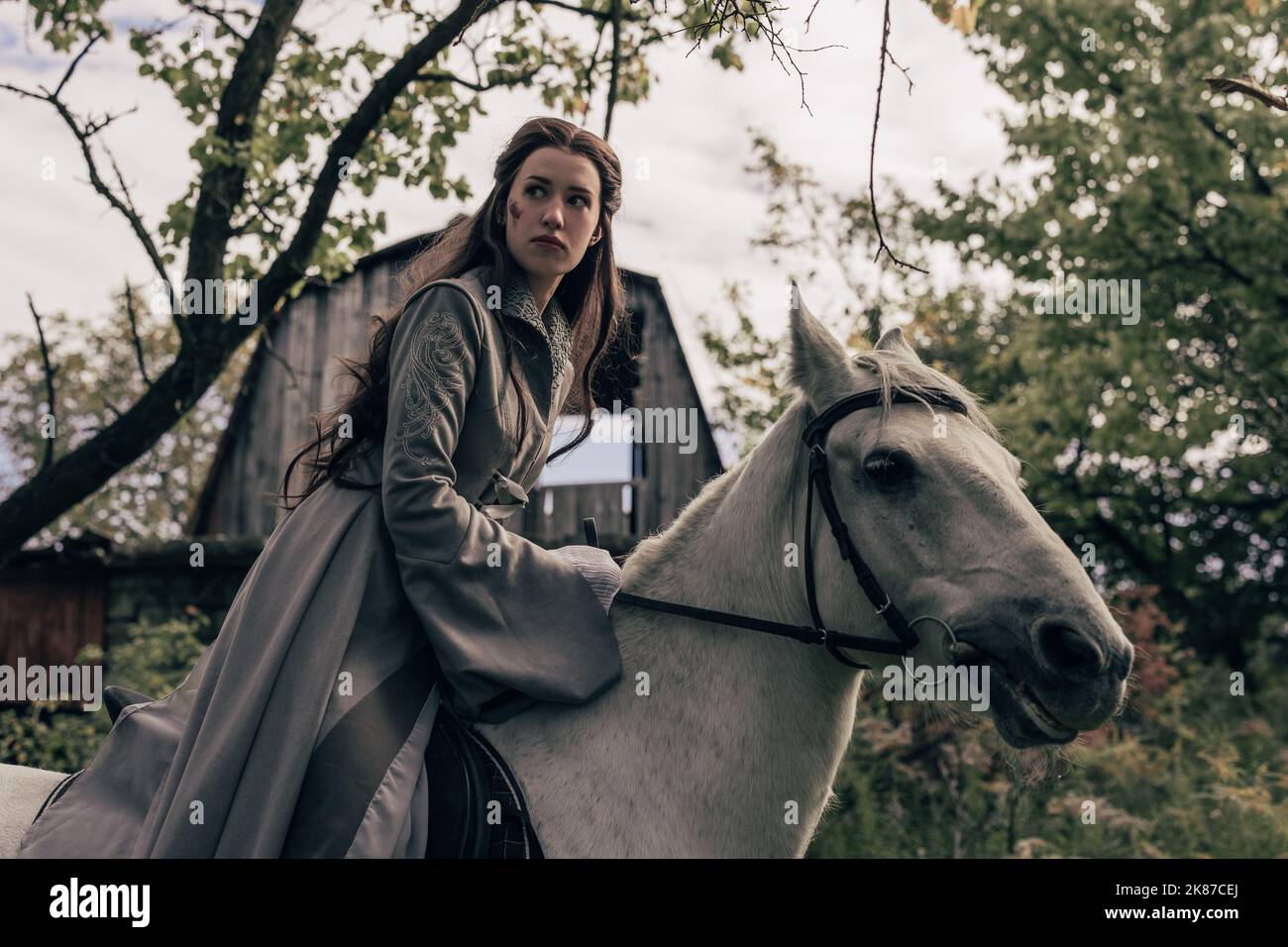 Young woman in image of ancient rider warrior sits on white horse in ...