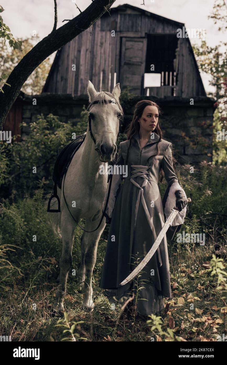 Young woman in image of ancient rider warrior stands near white horse ...