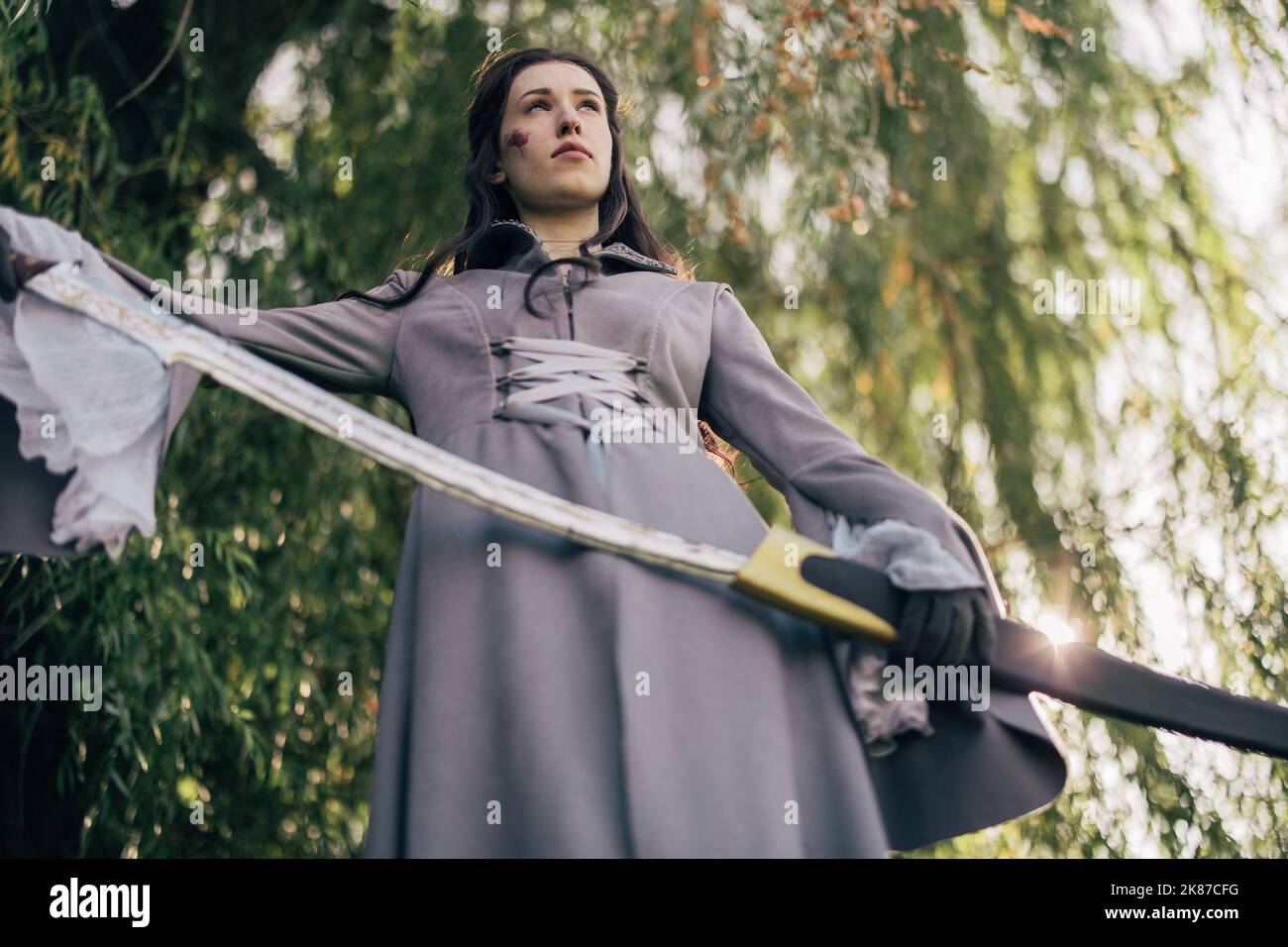 Young woman in image of ancient warrior stands under tree with sword in ...