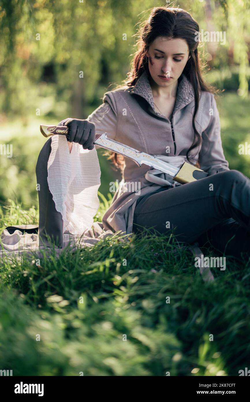 Young woman in image of ancient warrior sits and rests on grass under ...