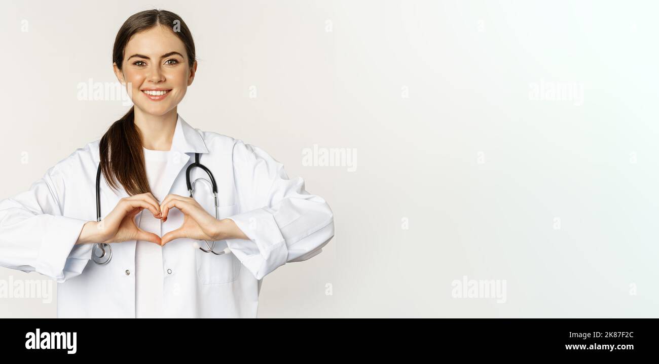 Portrait of smiling doctor, female physician showing heart sign and ...