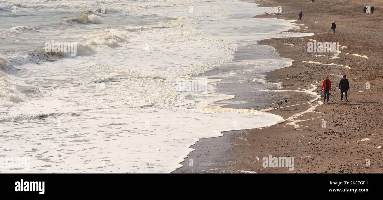 People walking on the beach as foam collects on an incoming tide Stock ...