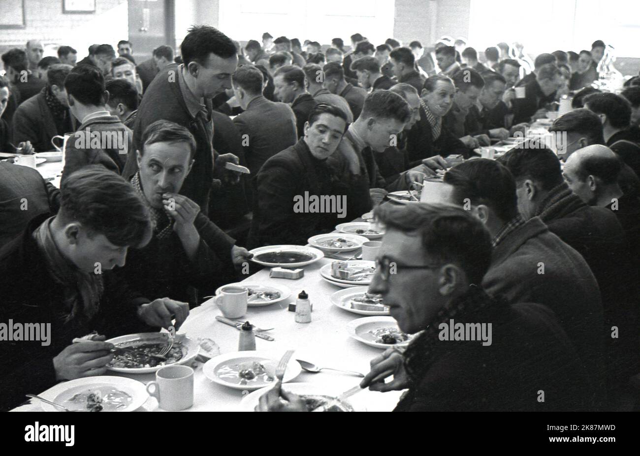 1937, historical, male workers sitting together at long tables eating a ...