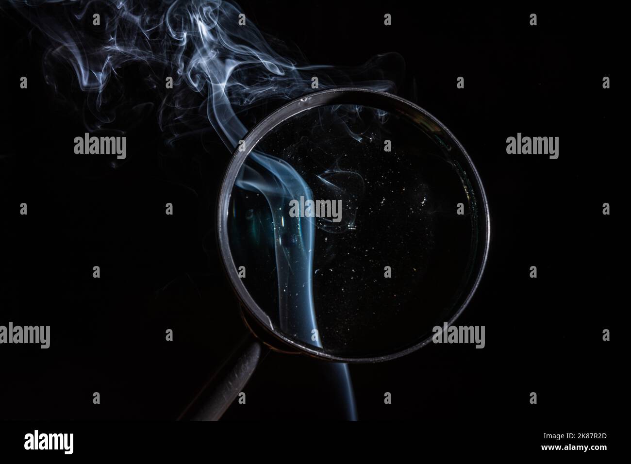 A magnifying glass against a black background and smoke coming from ...