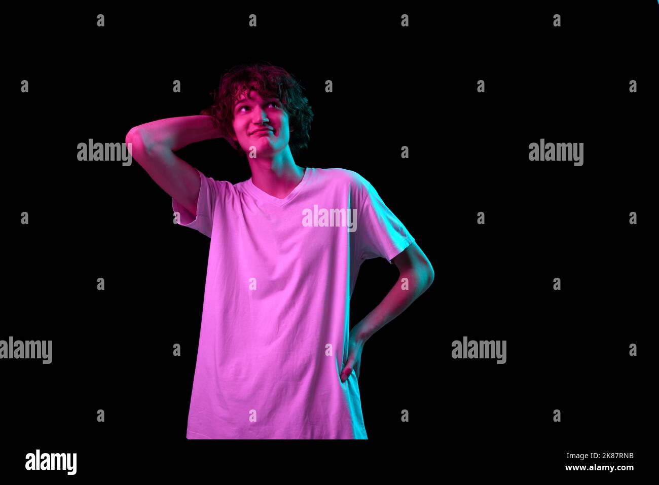 Smiling young man looking up dreamily isolated over dark background in ...