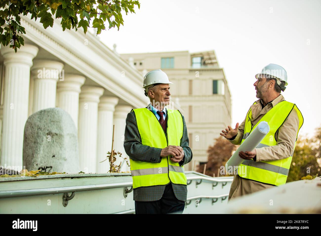 Two senior construction managers are standing and talking about the ...