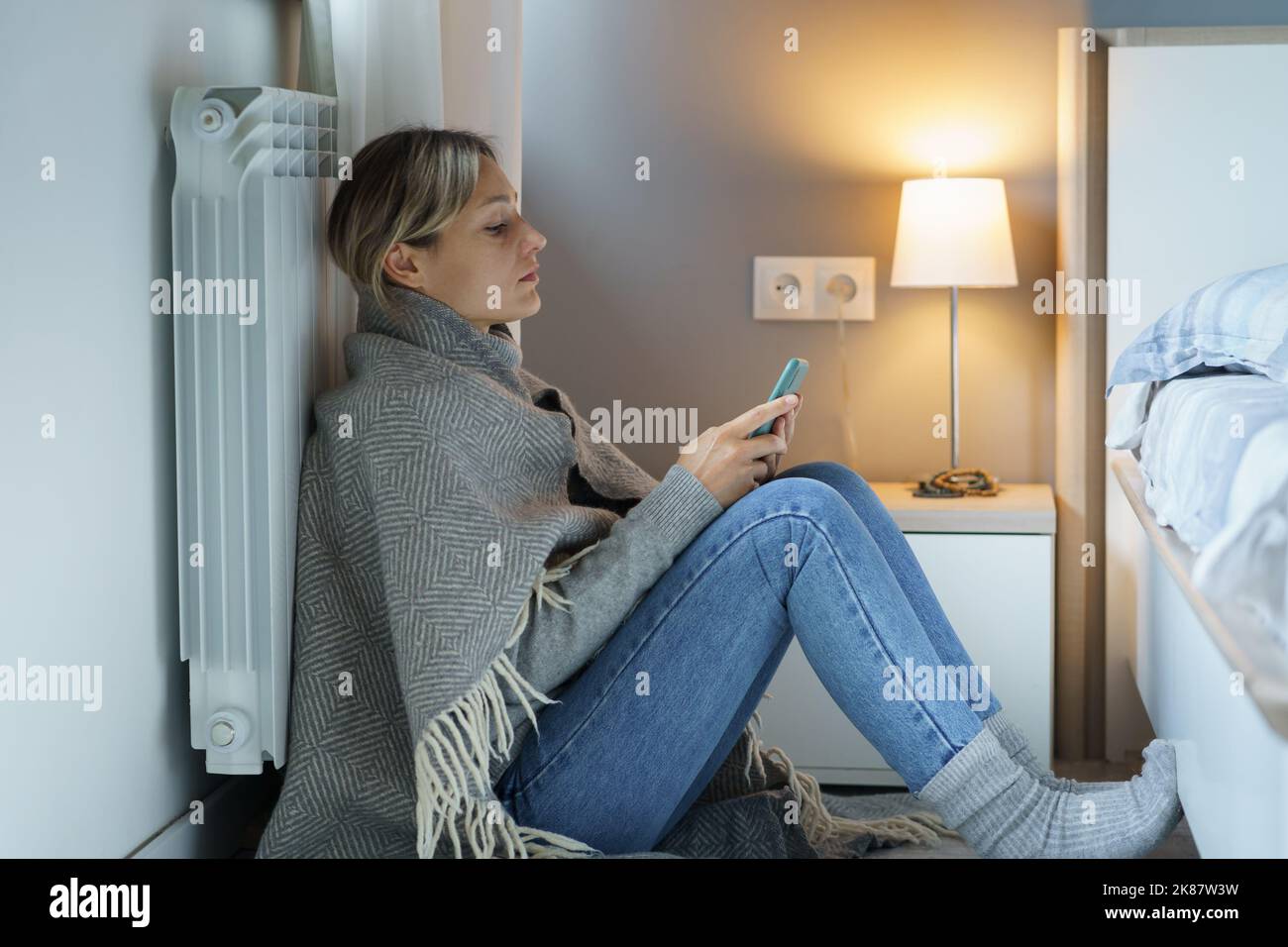 Tired blonde woman snuggling up to battery scrolls smartphone looking ...