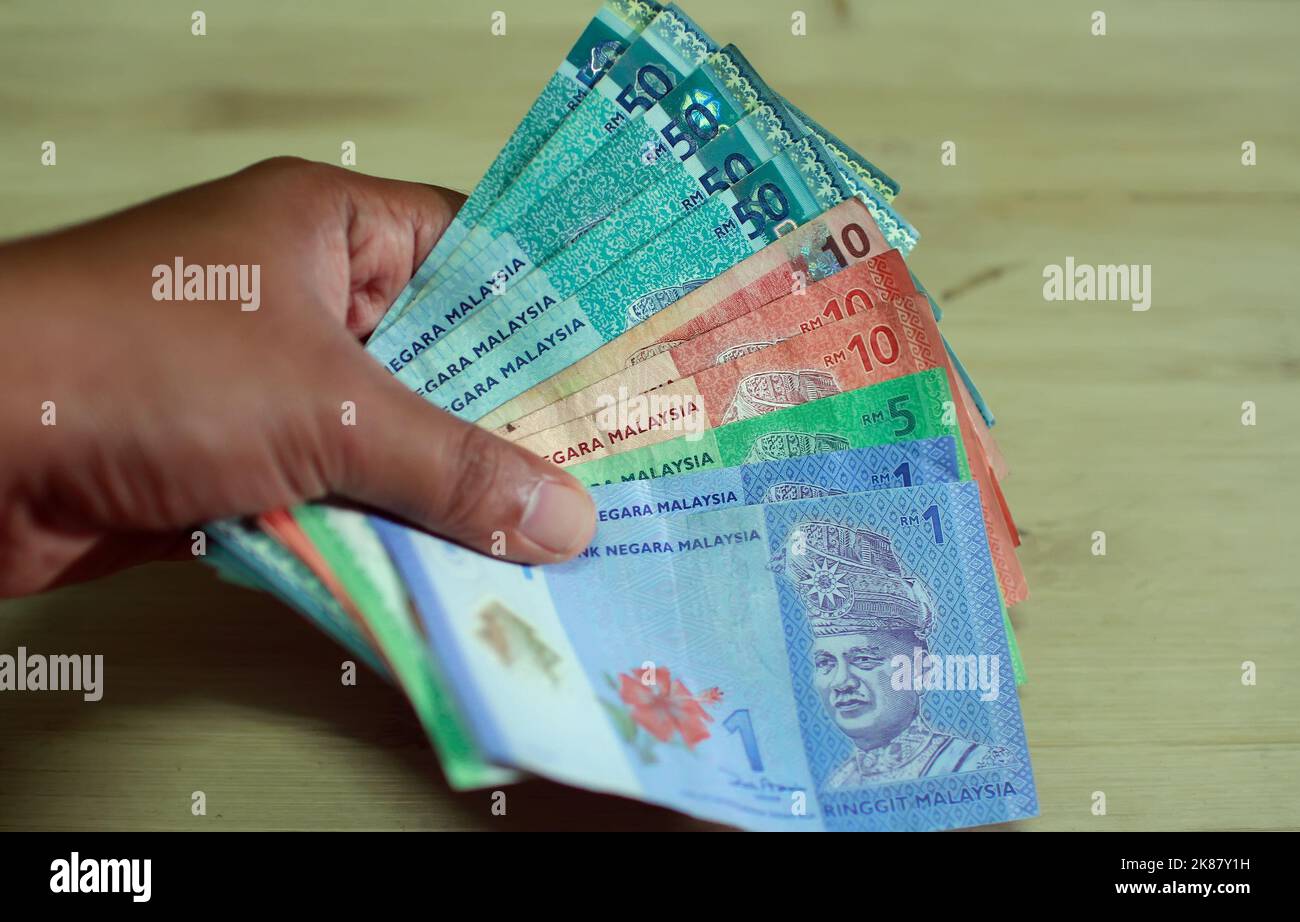 A man holding a lot of Malaysian colorful banknotes in ascending order ...