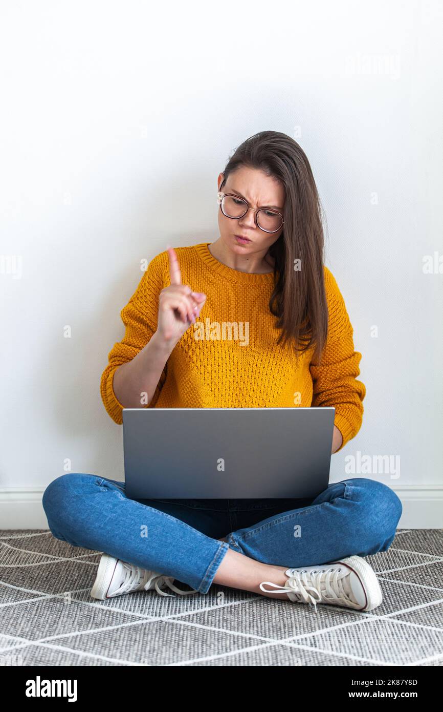 Young woman tired, angry using laptop sitting on carpet on white ...