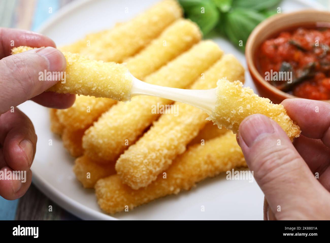 Breaking freshly fried mozzarella sticks and stretching cheese with ...