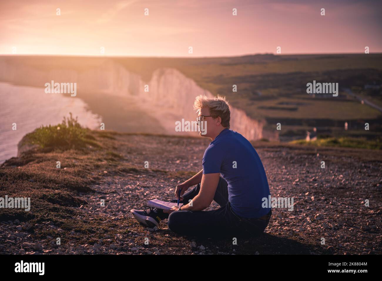 A man sitting on a rocky cliff watching the Seven Sisters cliffs in ...