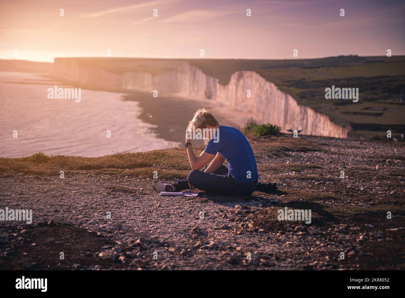 A man sitting on a rocky cliff watching the Seven Sisters cliffs in ...