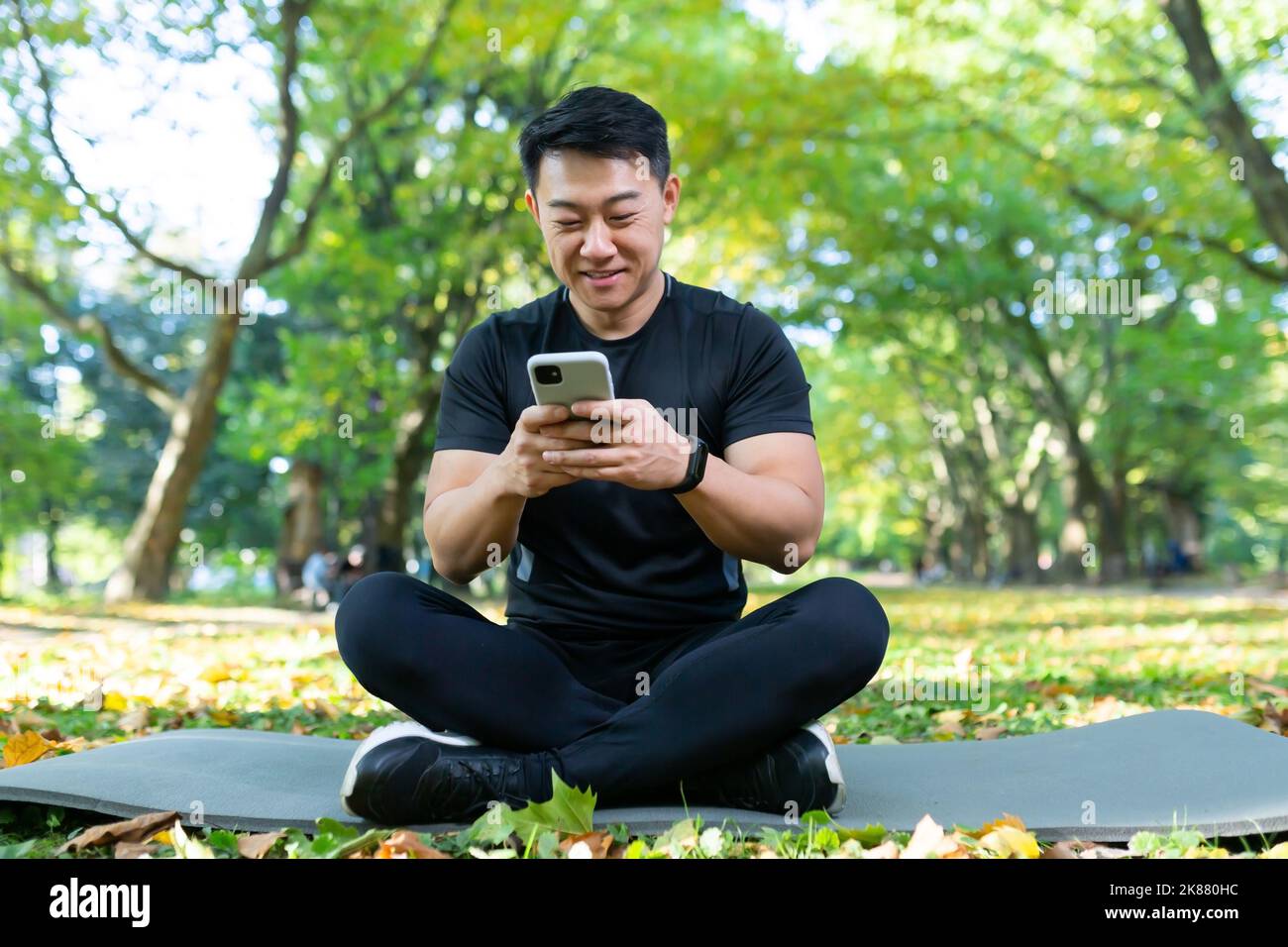 Sportsman in lotus pose sitting on sports mat in park and smiling ...