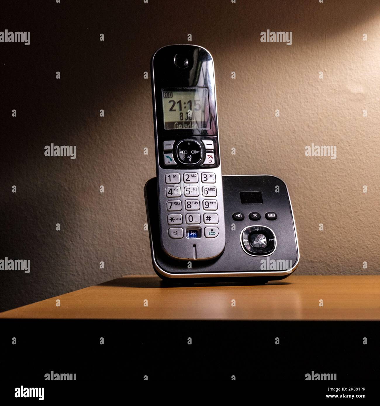 A wireless black telephone with cradle on the table in the dark room ...