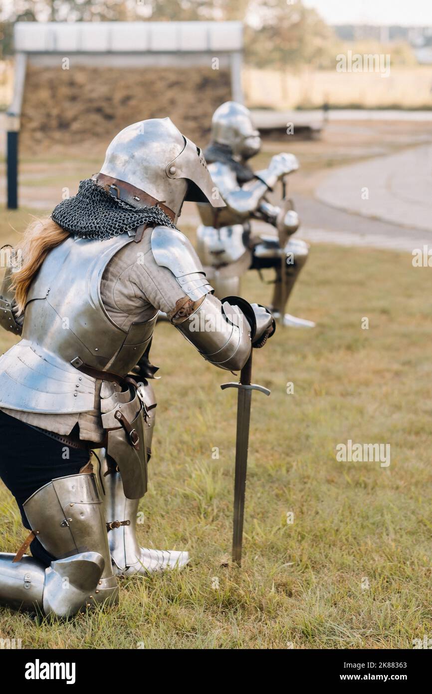 two knights in ancient metal armor stand at the stone wall of the ...