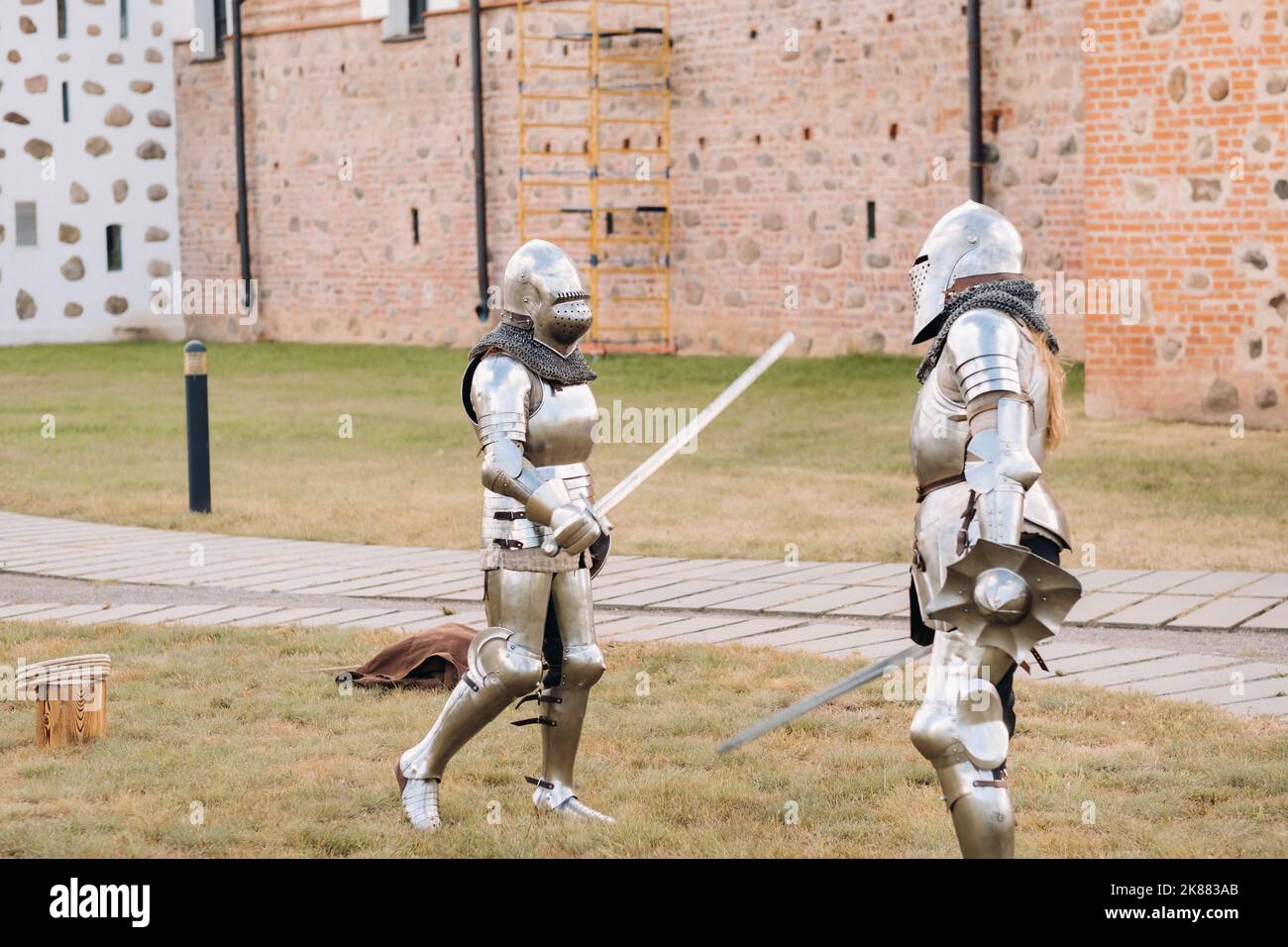 two knights in ancient metal armor are standing at the stone wall of ...