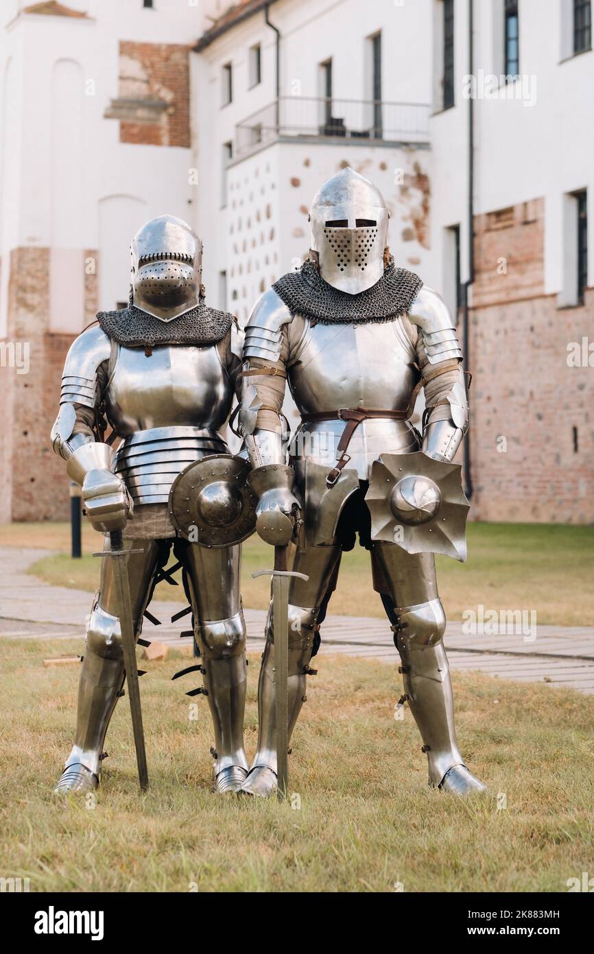 two knights in ancient metal armor stand at the stone wall of the ...