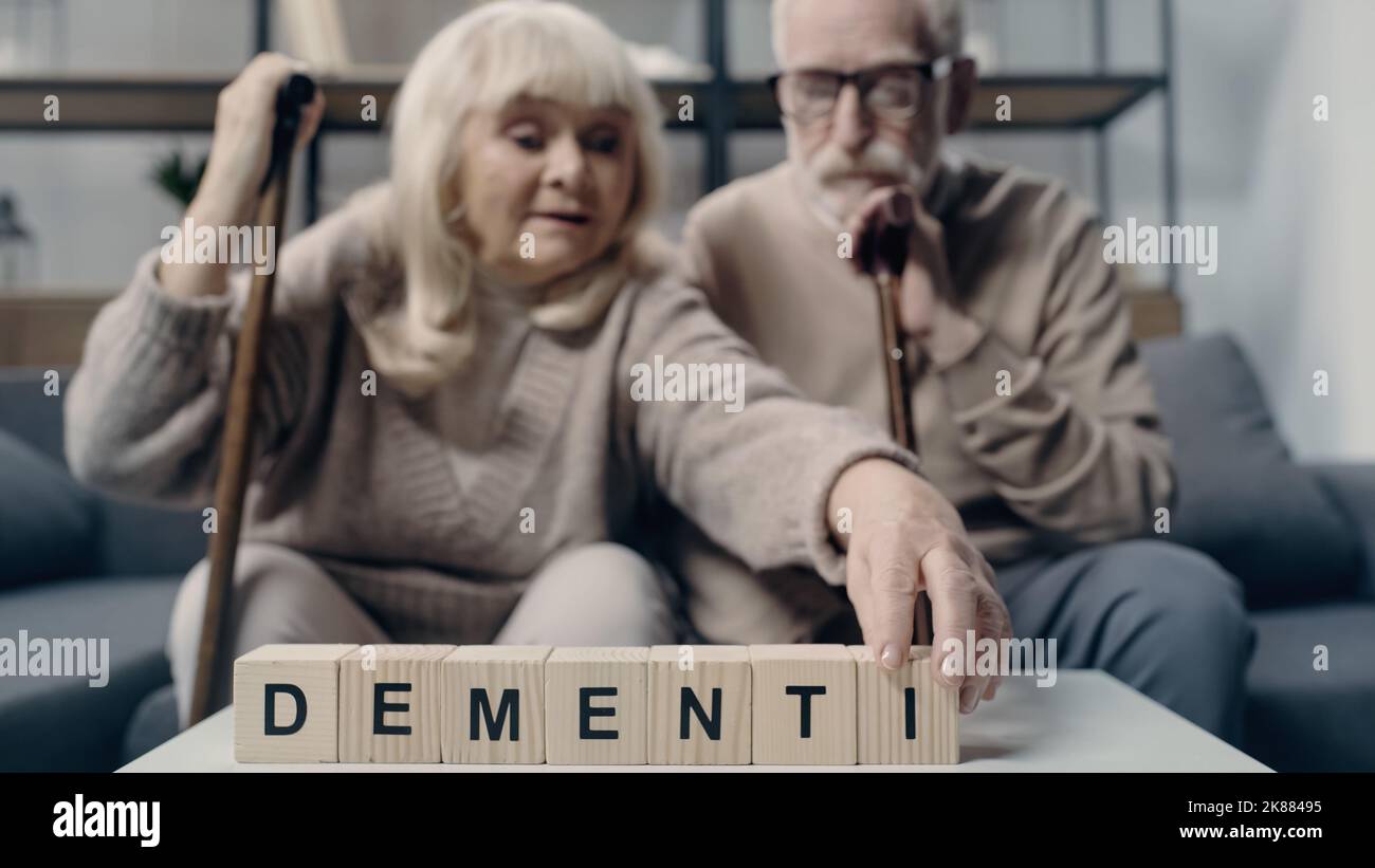 Senior man sitting near woman putting wooden cube with lettering and ...