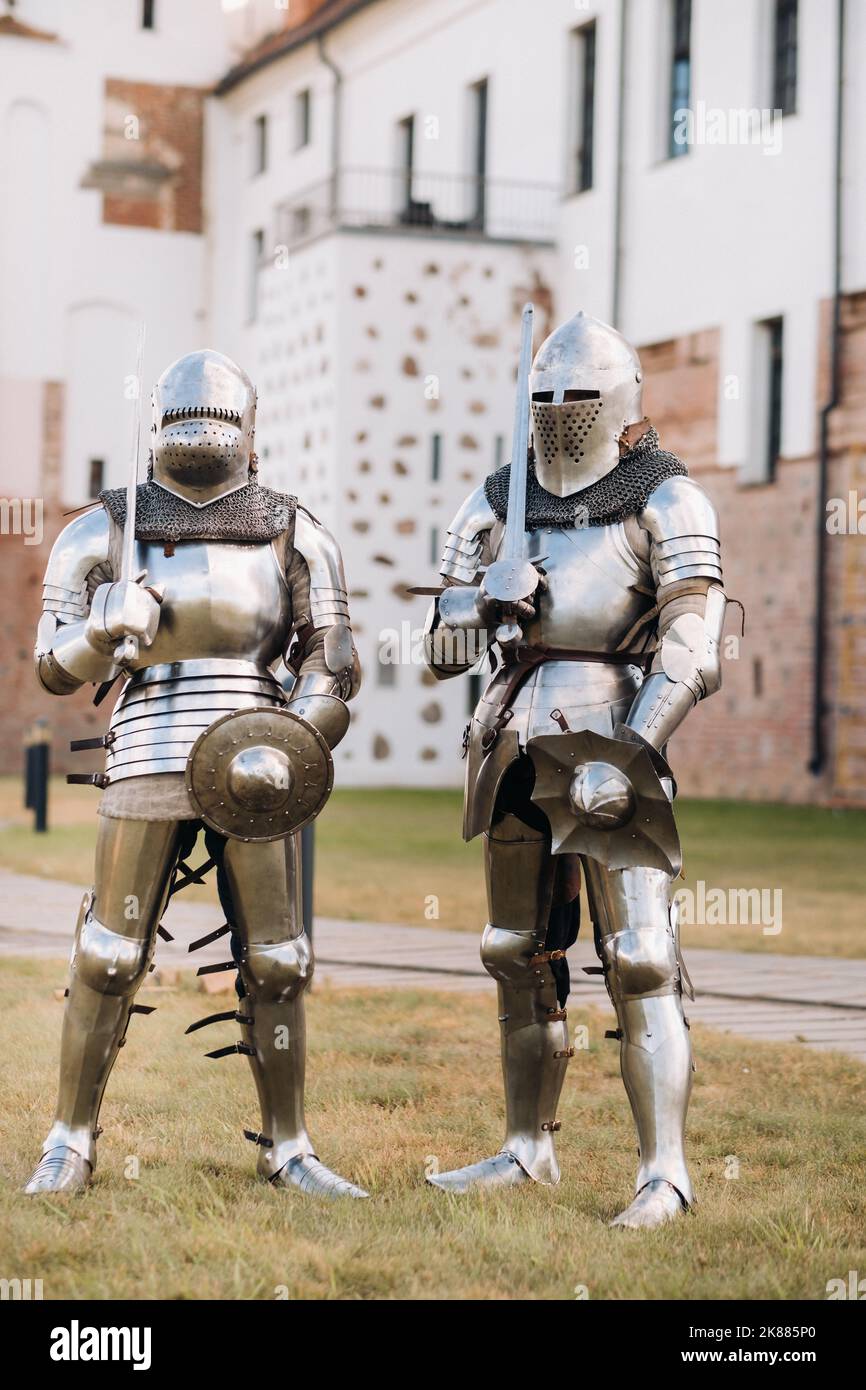 two knights in ancient metal armor stand at the stone wall of the ...