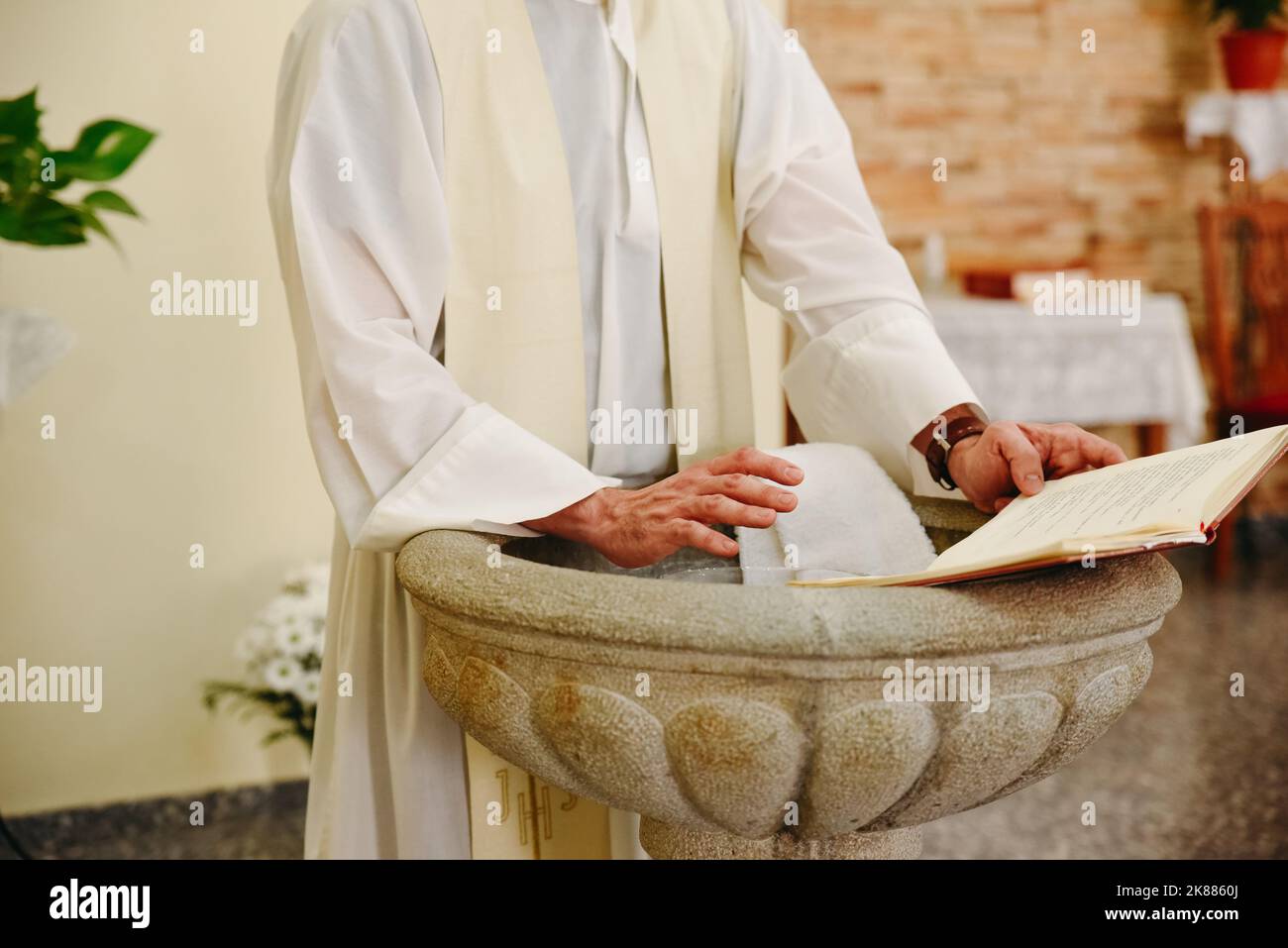 A priest with a white robe standing in front of a baptismal font with a ...