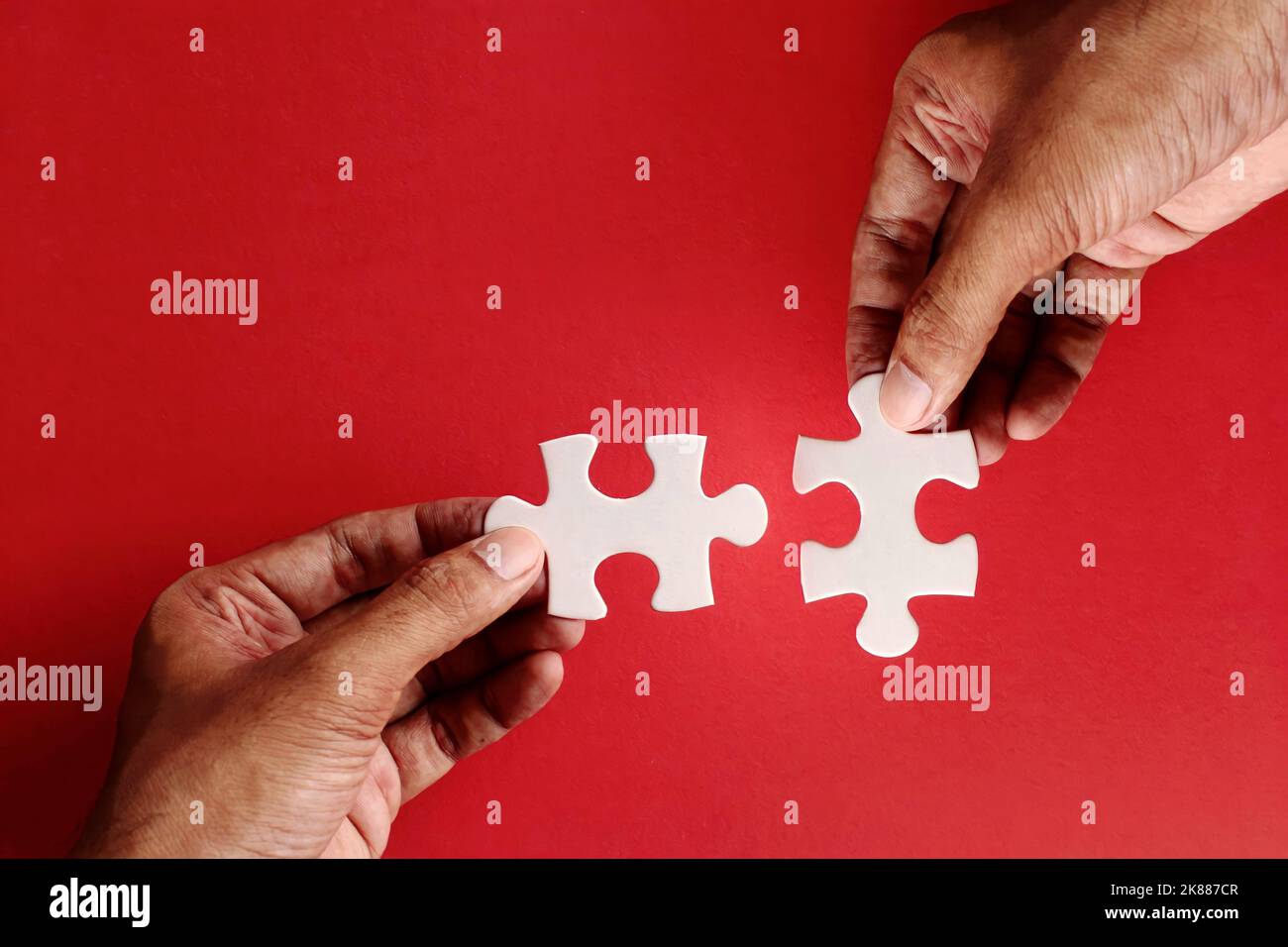 Two hands connect puzzle piece on red background. Teamwork, solutions ...