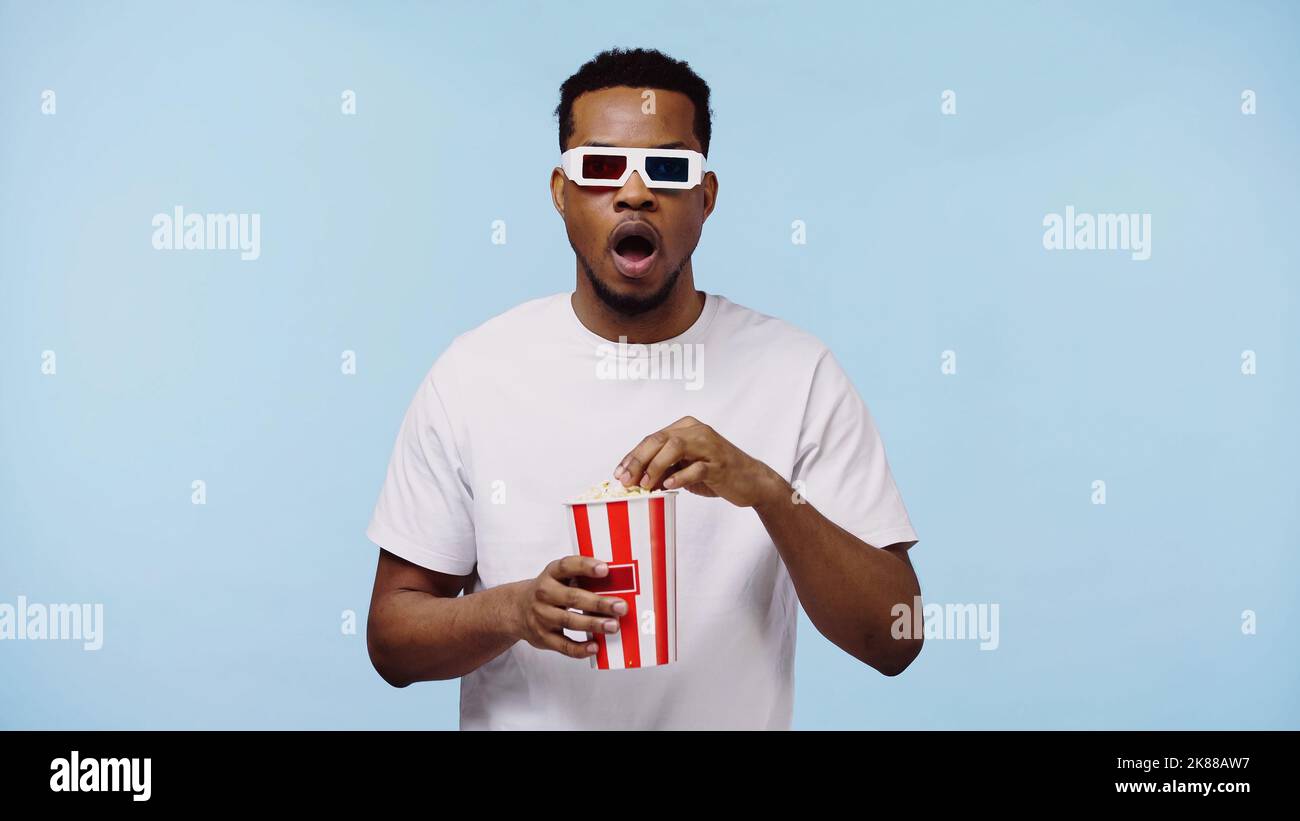 surprised african american man in 3d glasses watching movie and holding popcorn bucket isolated ...