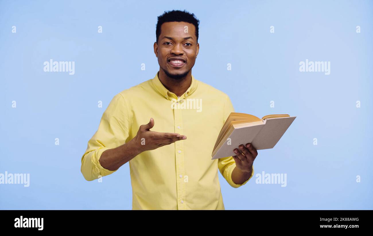 happy african american man in yellow shirt pointing at book isolated on ...