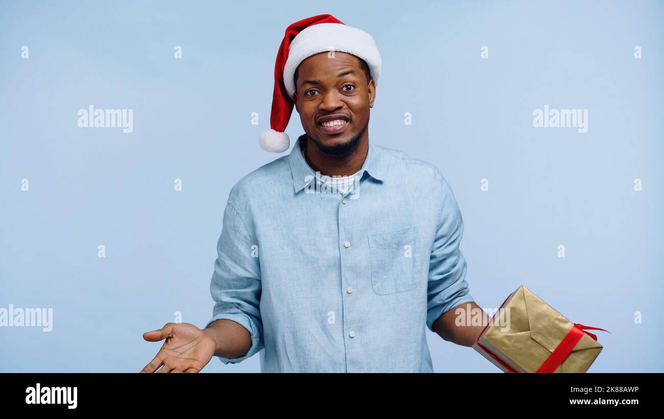 confused african american man in santa hat holding christmas gift box ...
